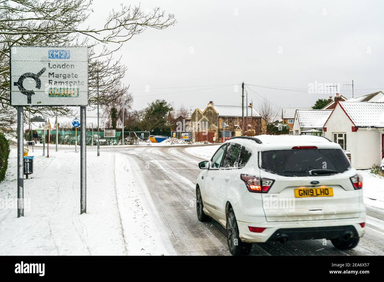 A blue car approaching roundabout, during snowfall on a winter morning ...