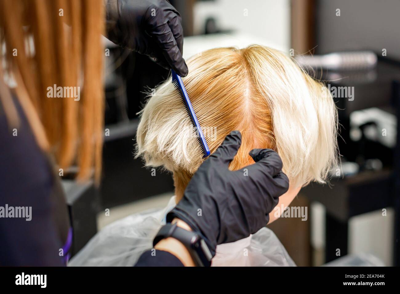 Hairdresser combing female short blonde hair before dyeing in a hair ...
