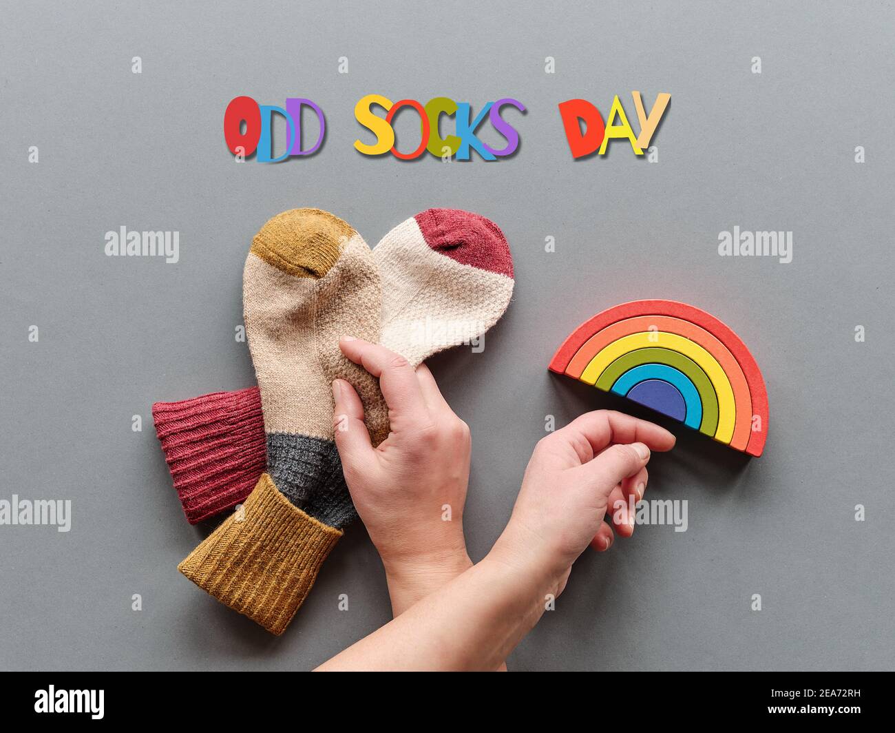 Odd Socks Day. Hand hold pair of mismatched socks. Wooden rainbow, toy ...