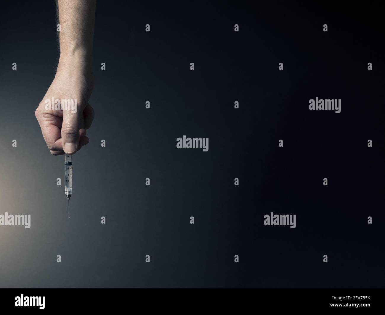 Colour image of man's hand holding syringe vertically downwards with ...