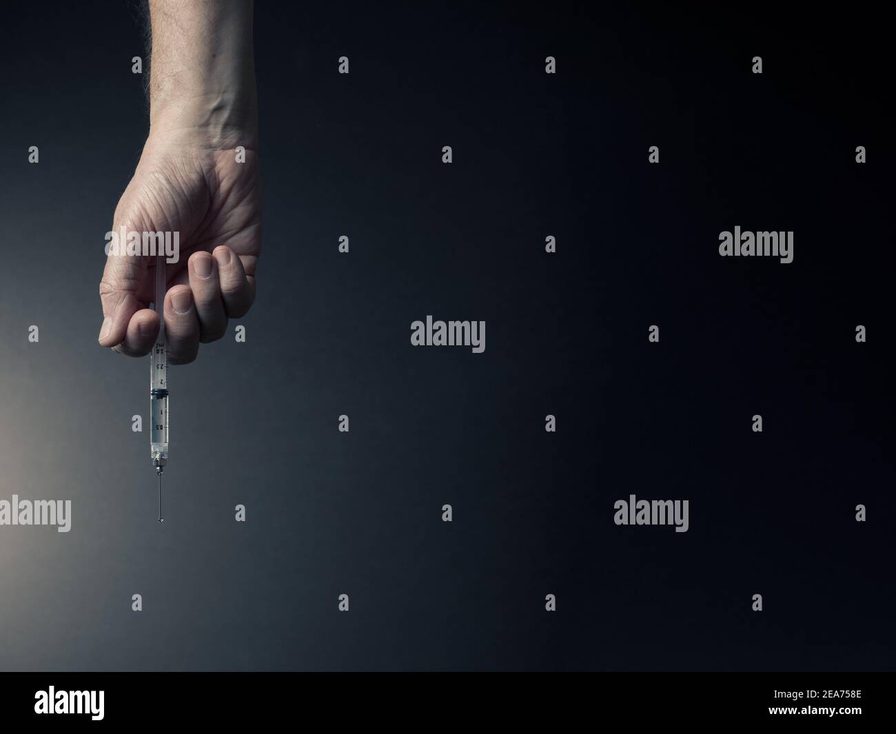 Colour image of man's hand holding syringe vertically downwards with ...