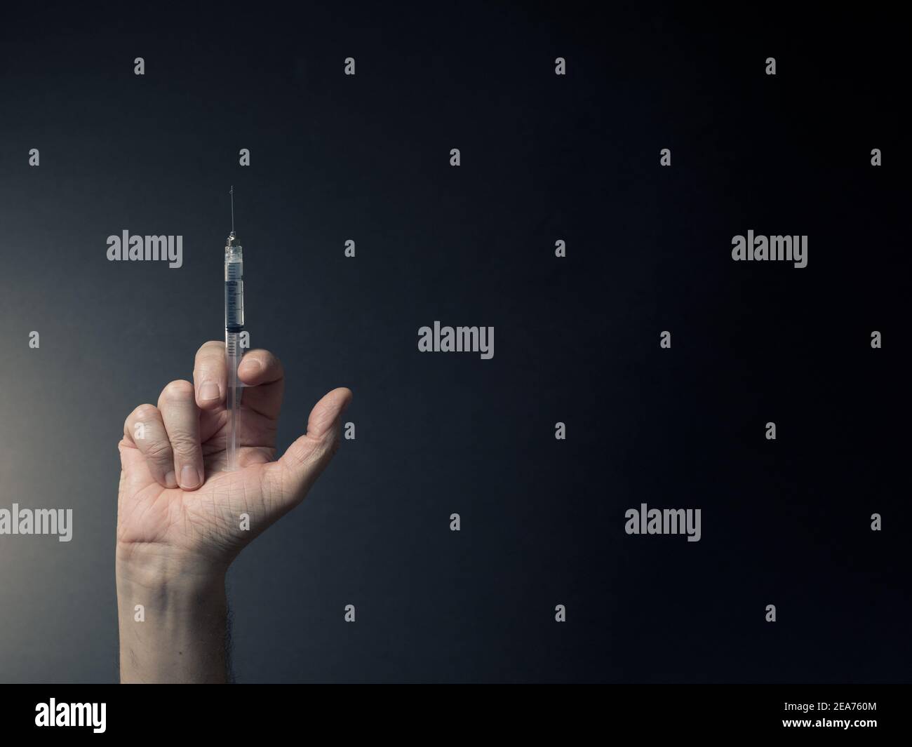 Colour image of man's open hand holding syringe vertically upwards with ...