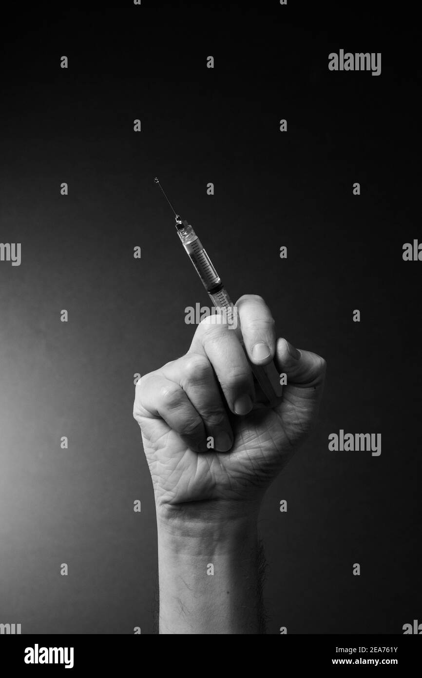 Black and white image of man's clenched hand holding syringe upwards ...