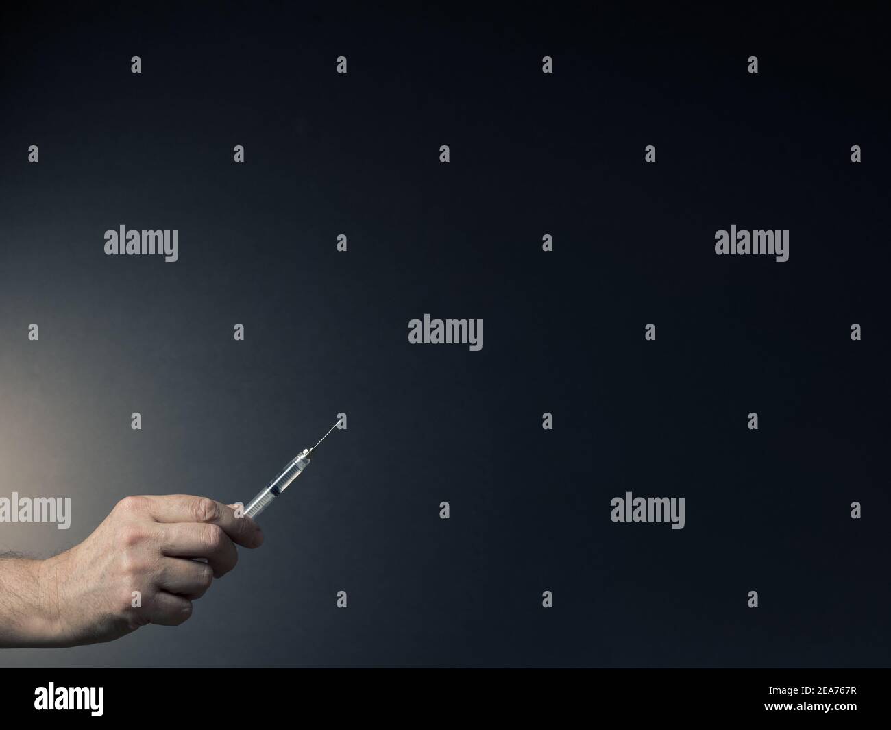 Colour image of man's hand holding syringe upwards in fingertips with ...