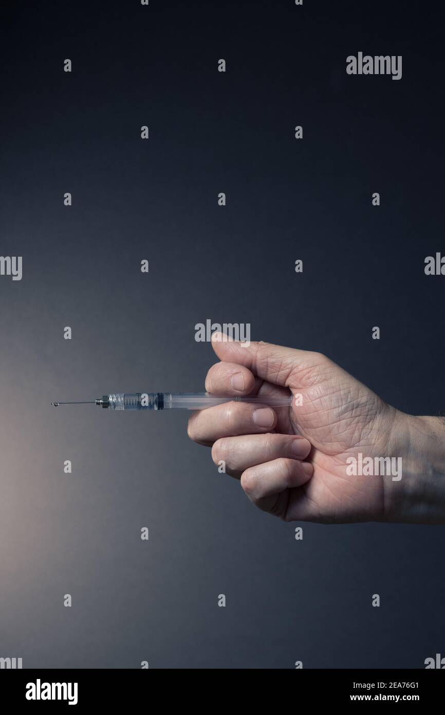 Colour image of man's clenched hand holding syringe horizontally with ...