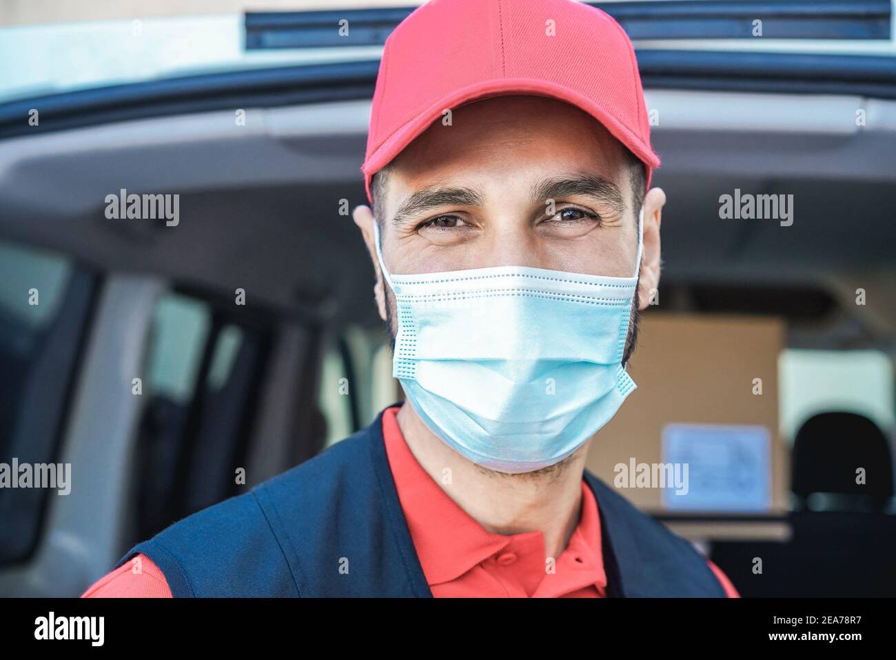 Hispanic delivery man smiling on camera while wearing safety mask ...