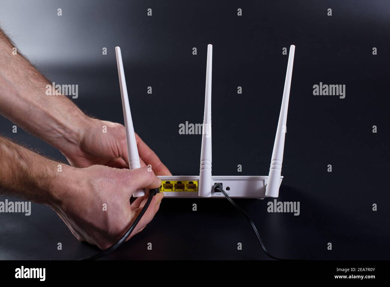 Hands connecting cable to white wifi router with three antennas.on ...