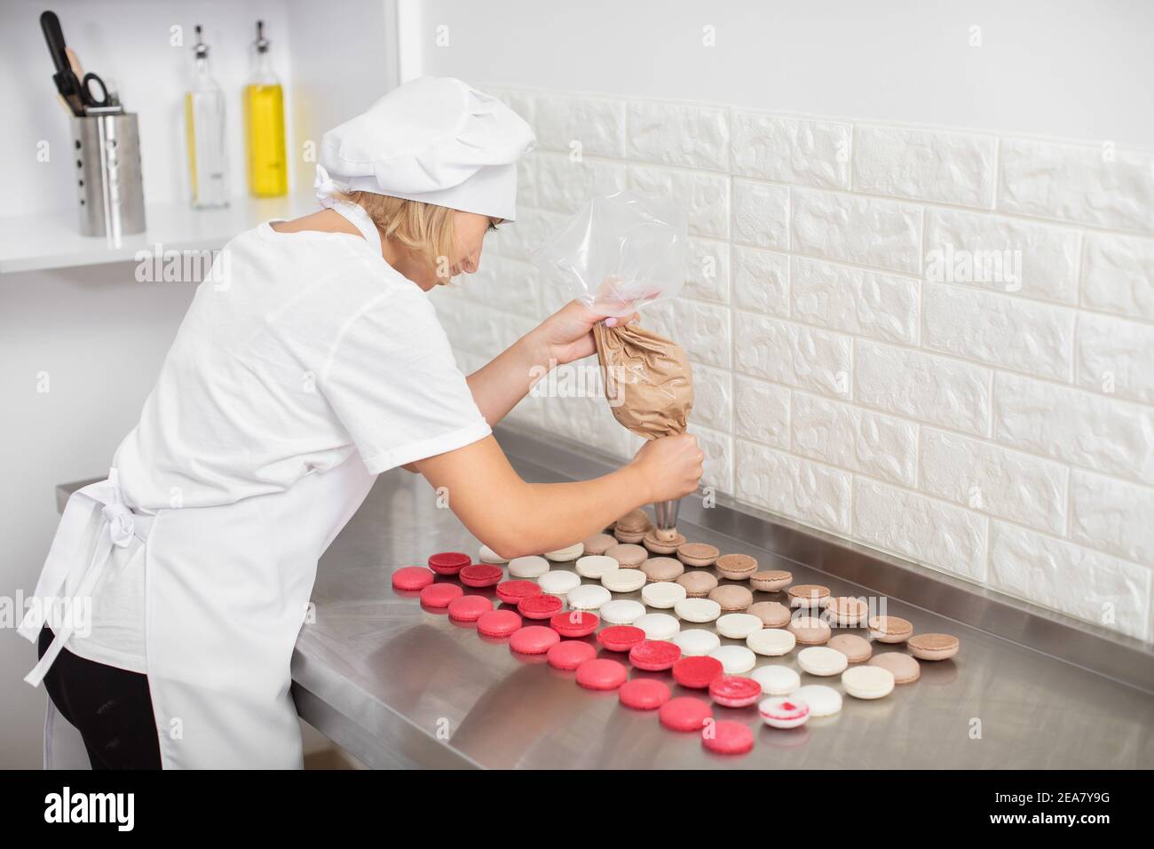 Concentrated female confectioner in white uniform making delicious ...