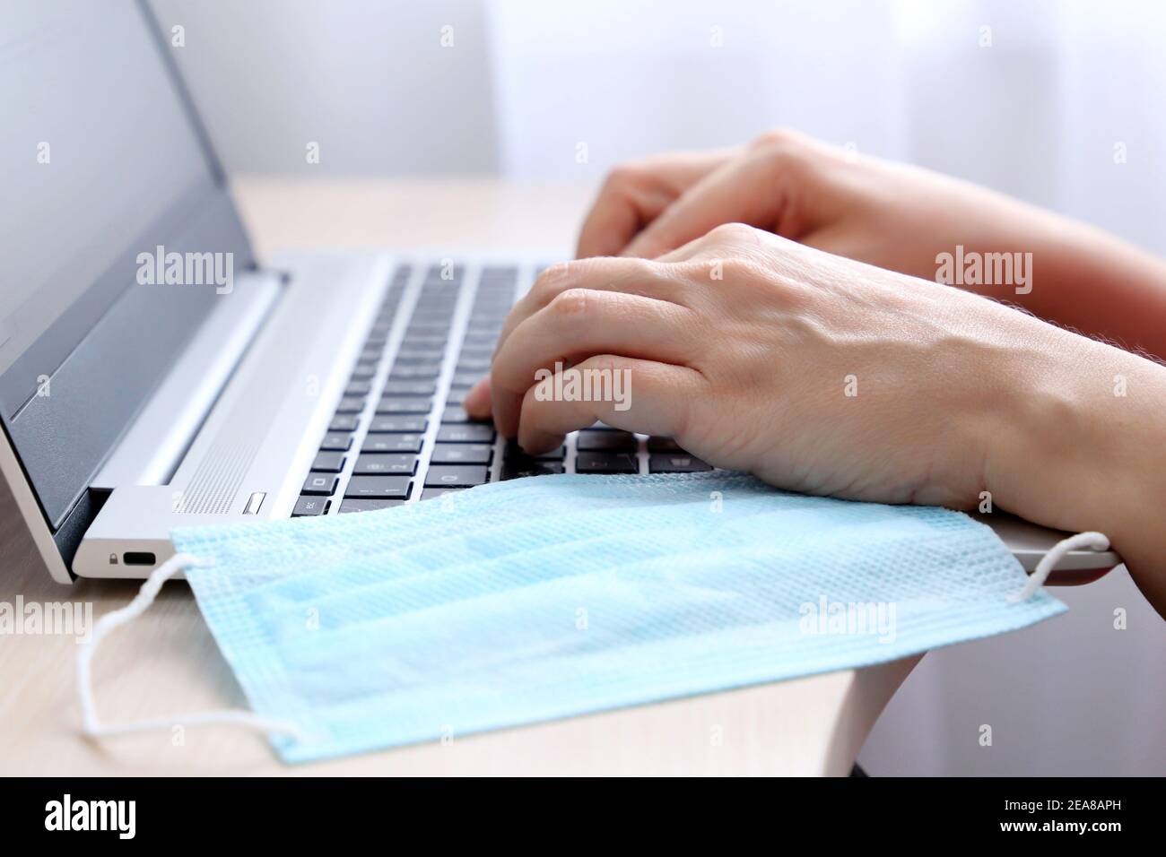 Female hands on laptop keyboard and removing medical mask on a desk ...