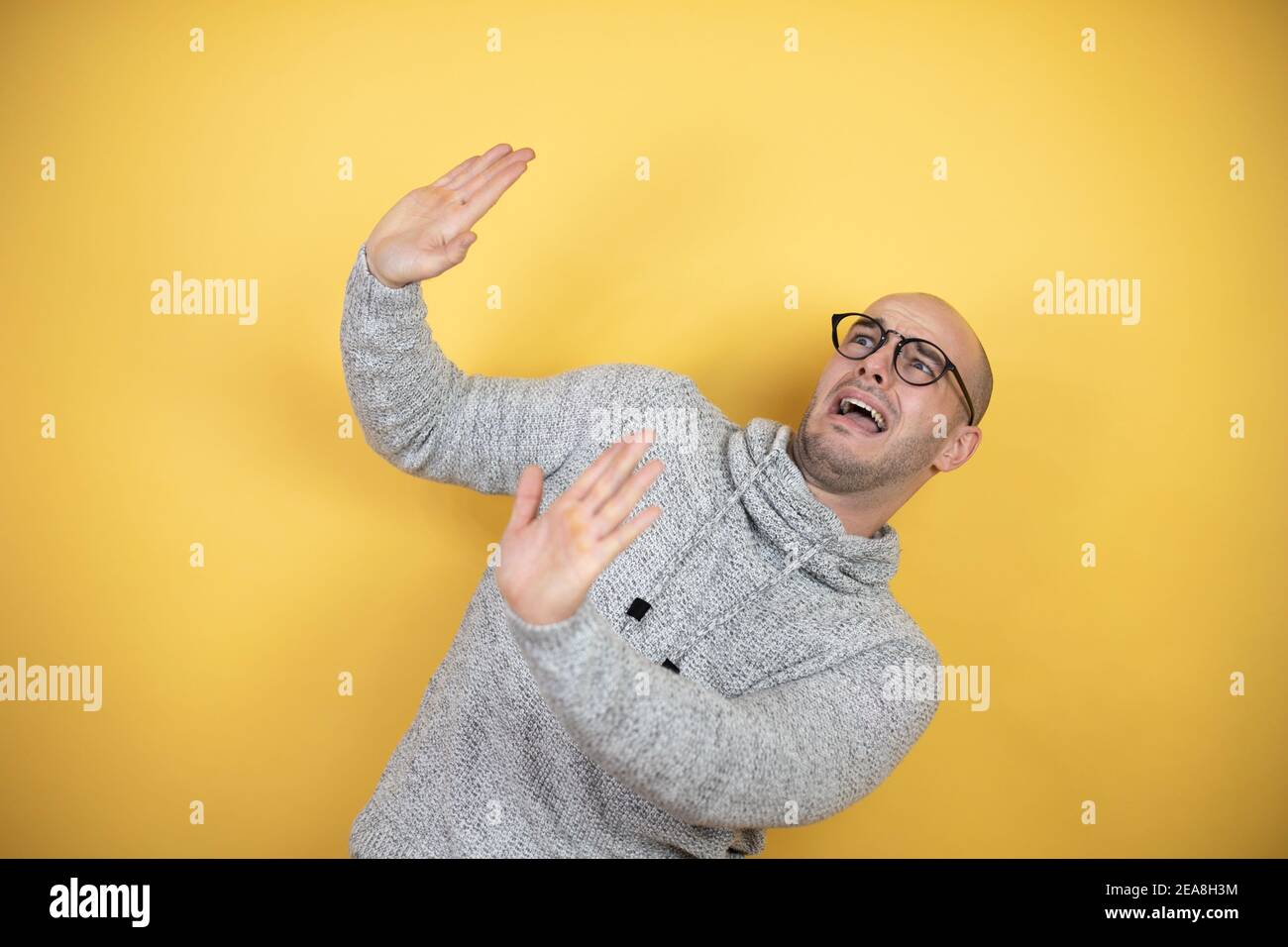 Young bald man wearing glasses over yellow background scared with his ...