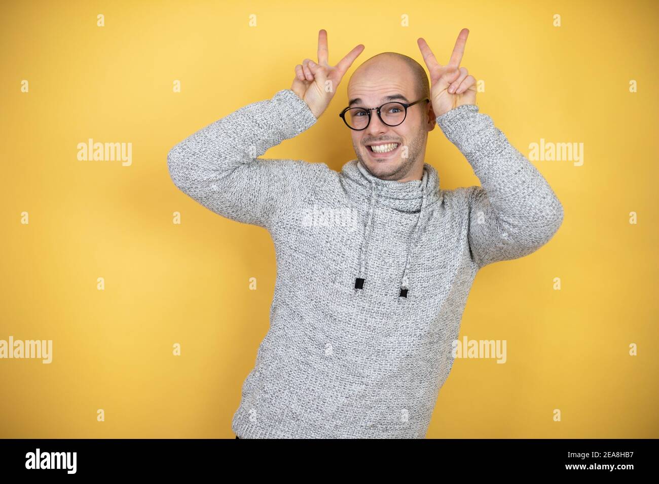Young bald man wearing glasses over yellow background Posing funny and ...