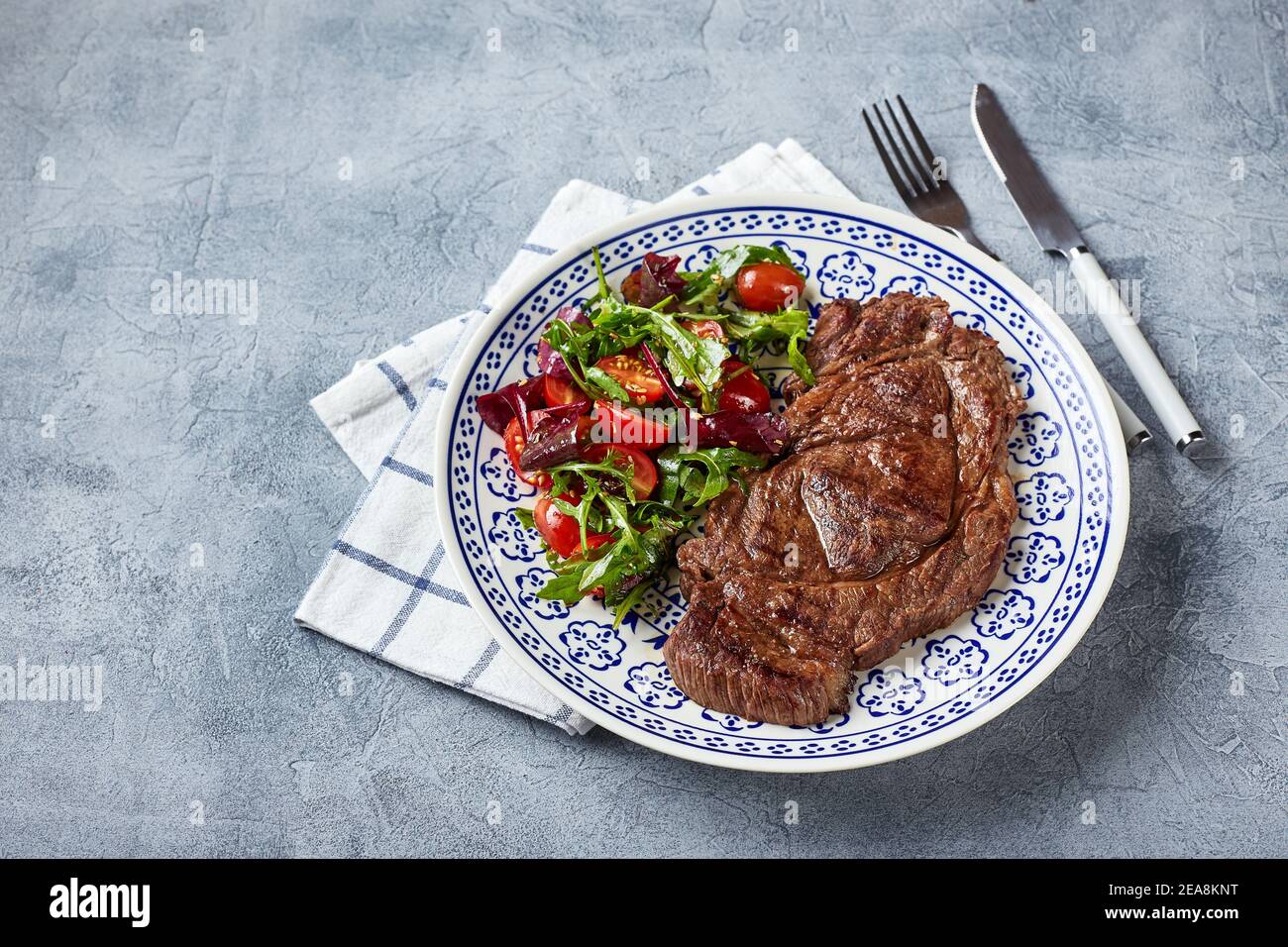 Grilled steaks and vegetable salad on light background. Table setting ...