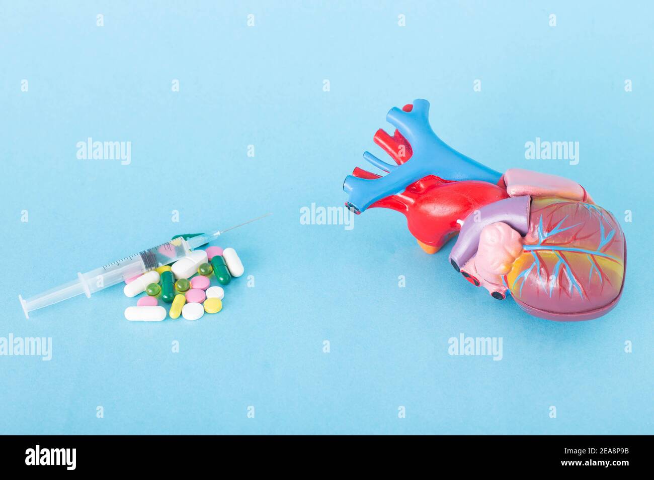 Mock up human heart on a blue background and a handful of pills with a ...