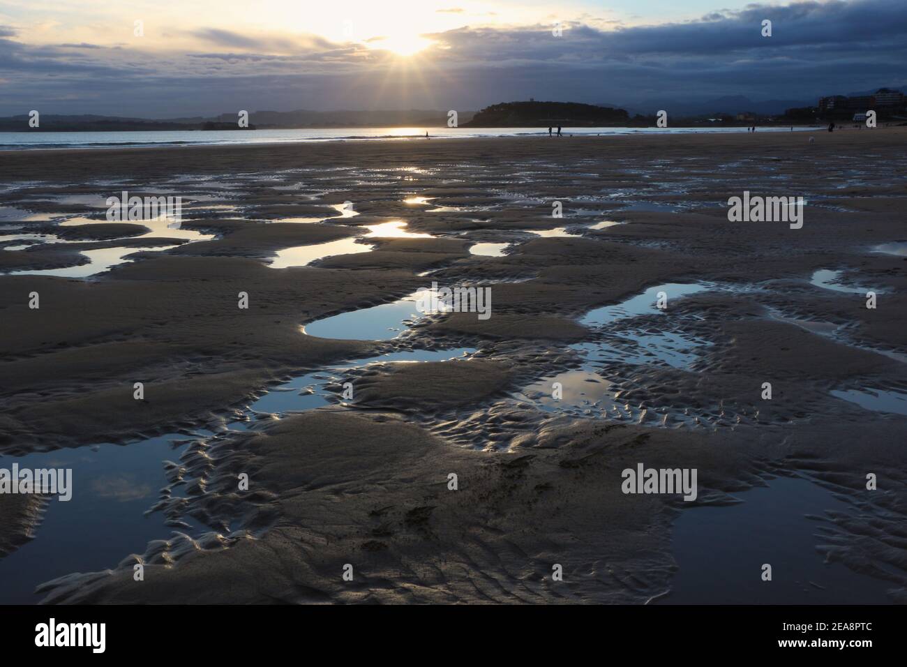 People on beach at low tide with a pattern of sand and sea water with ...