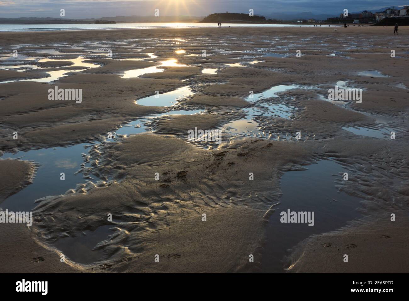 People on beach at low tide with a pattern of sand and sea water with ...