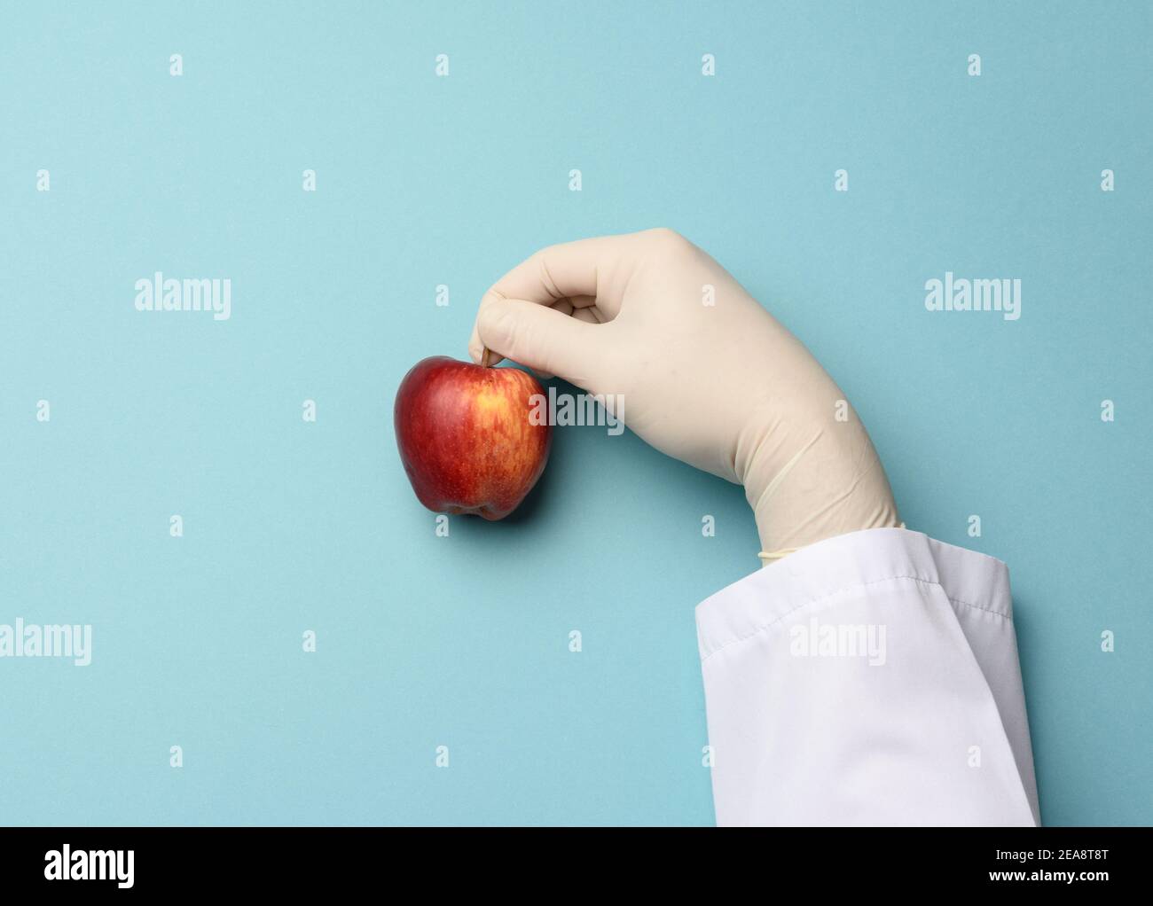 hand in a white latex glove holds a ripe red apple on a blue background ...