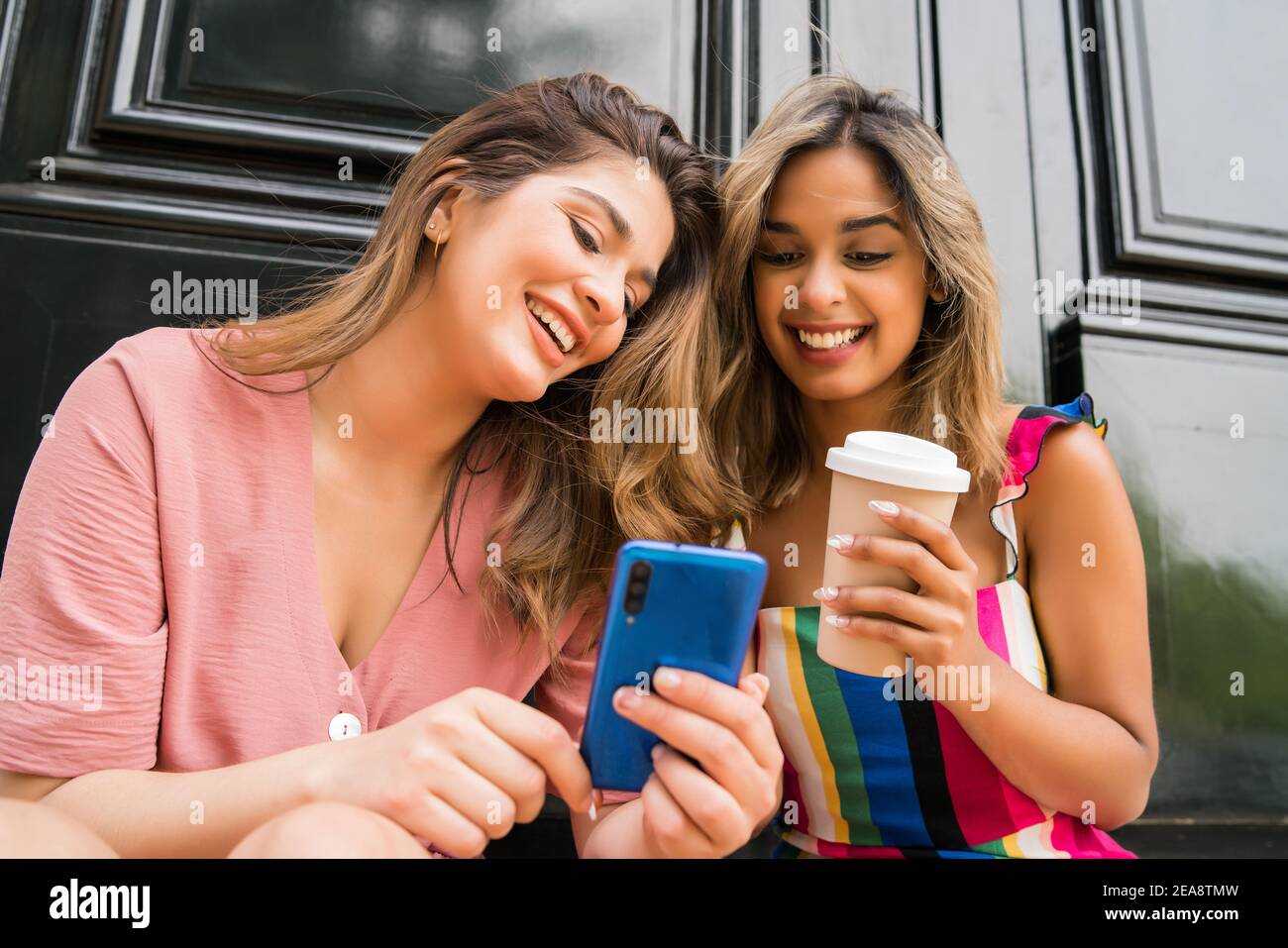 Two friends using mobile phone outdoors Stock Photo - Alamy