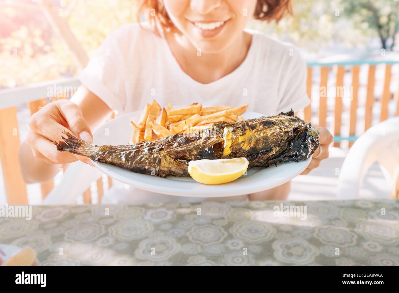 Smiling woman eating fresh river rainbow trout baked according to an ...