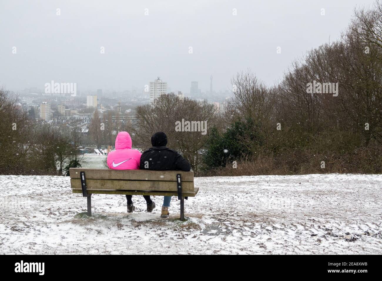 A couple sitting on a wooden park bench looking at the view of London ...