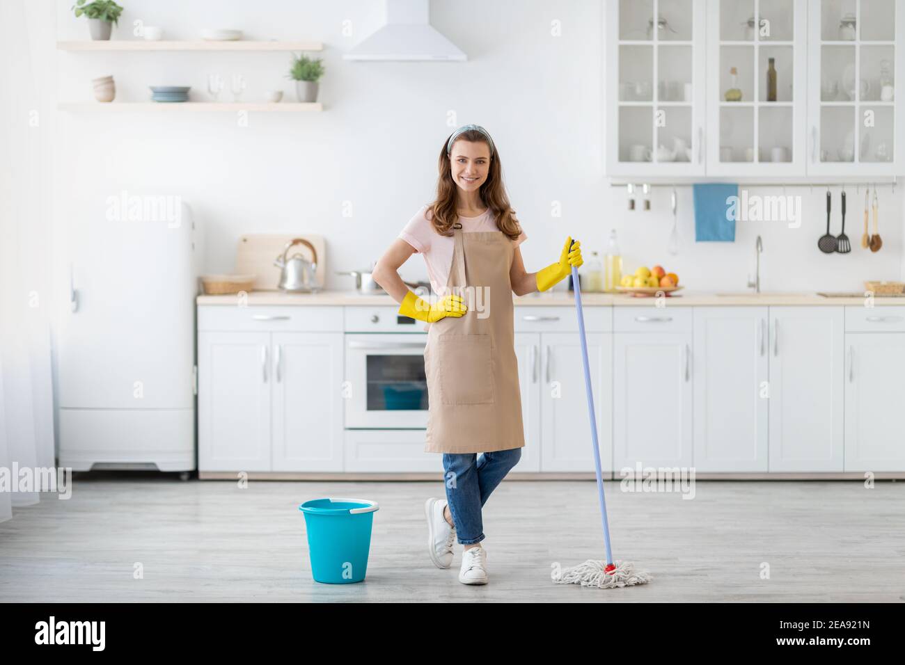 Full length portrait of happy young lady with mop washing floor in ...