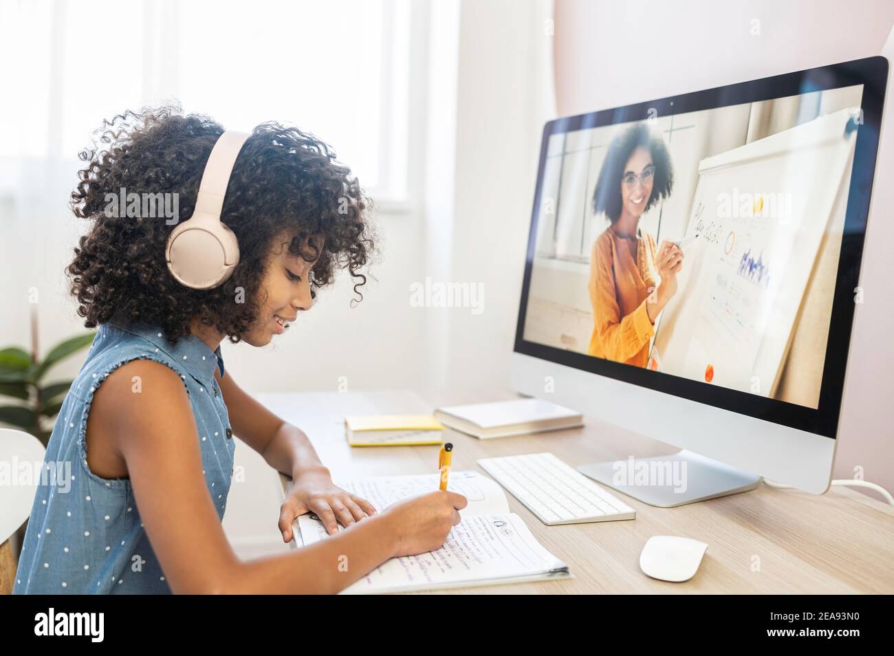 A clever multiethnic girl sits at table with a headphones, studying on ...