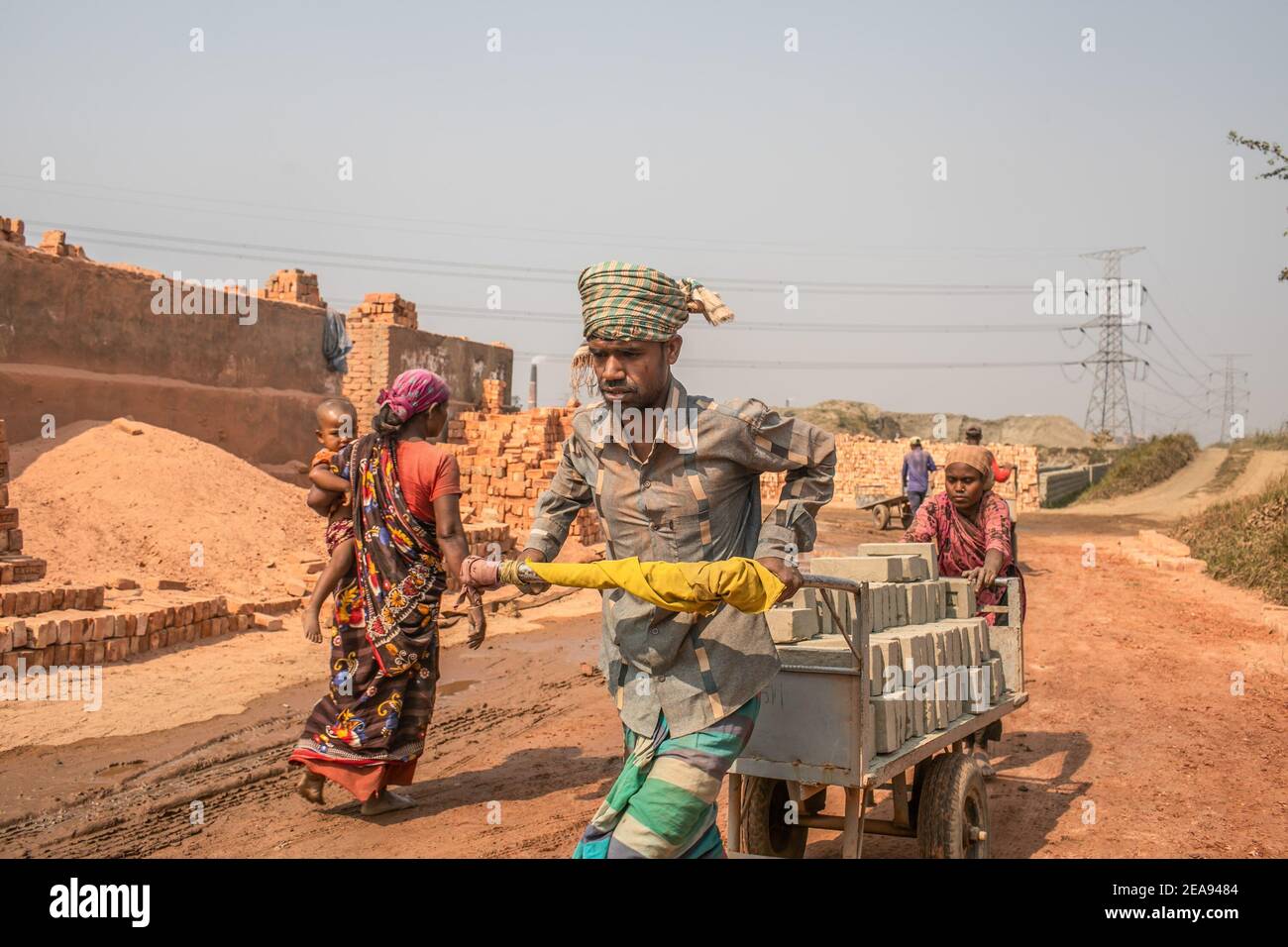 A labourer pulling a cart loaded with bricks ready to be burnt at a ...