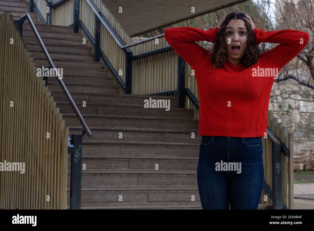 Beautiful woman in a red sweater grabbing her head in shock at a public ...