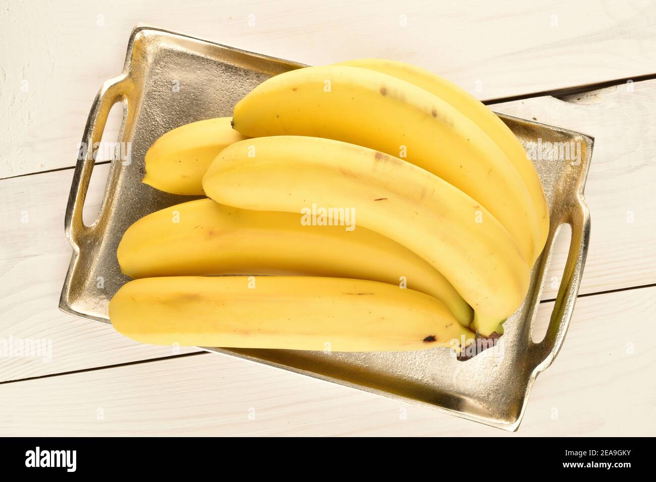 Several bright yellow ripe juicy organic bananas, on a metal tray ...