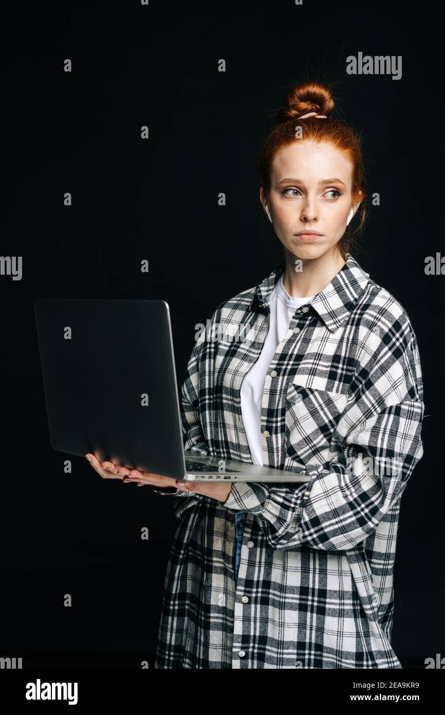 Upset young woman holding laptop computer wearing wireless earphones ...