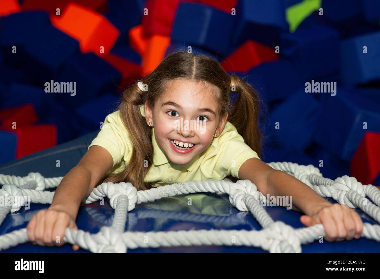 Cheerful teenage girl climbing rope ladder over foam cube pit at indoor ...