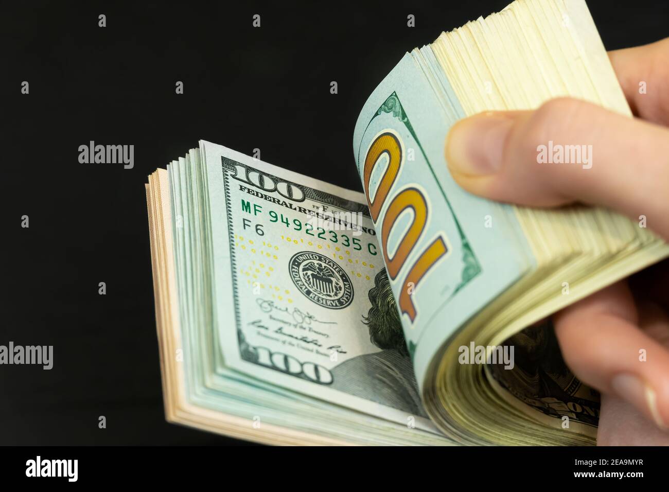 Women's hands move through a stack of hundred-dollar bills on a dark ...