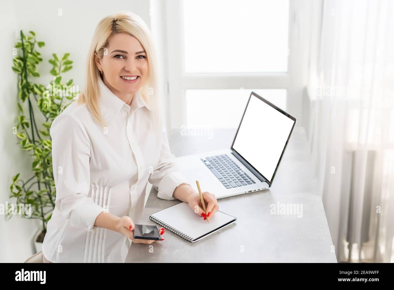 Young woman with laptop writes in notepad Stock Photo - Alamy