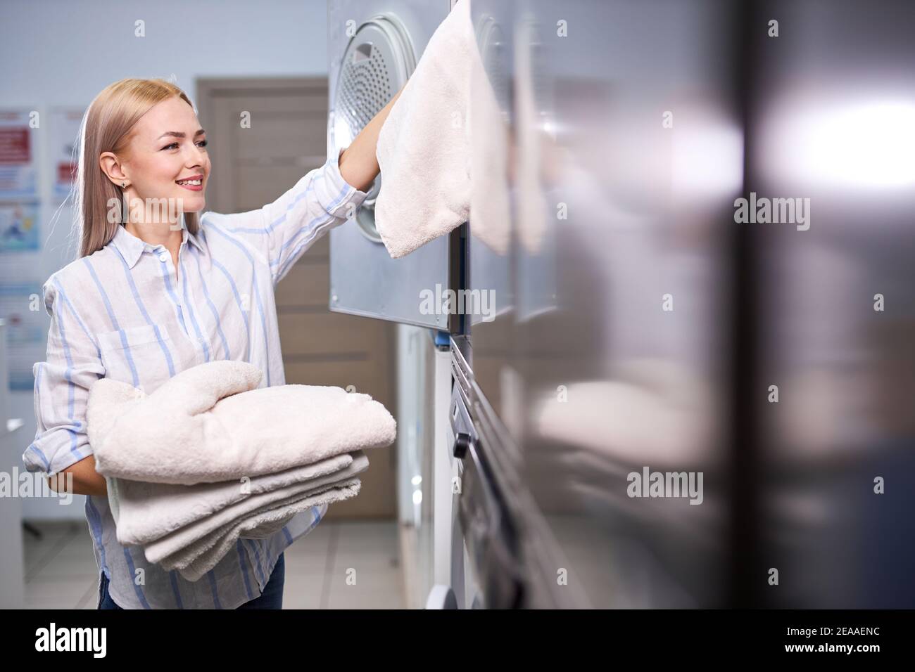 woman loading linen towels into washing machine, young caucasianfemale ...