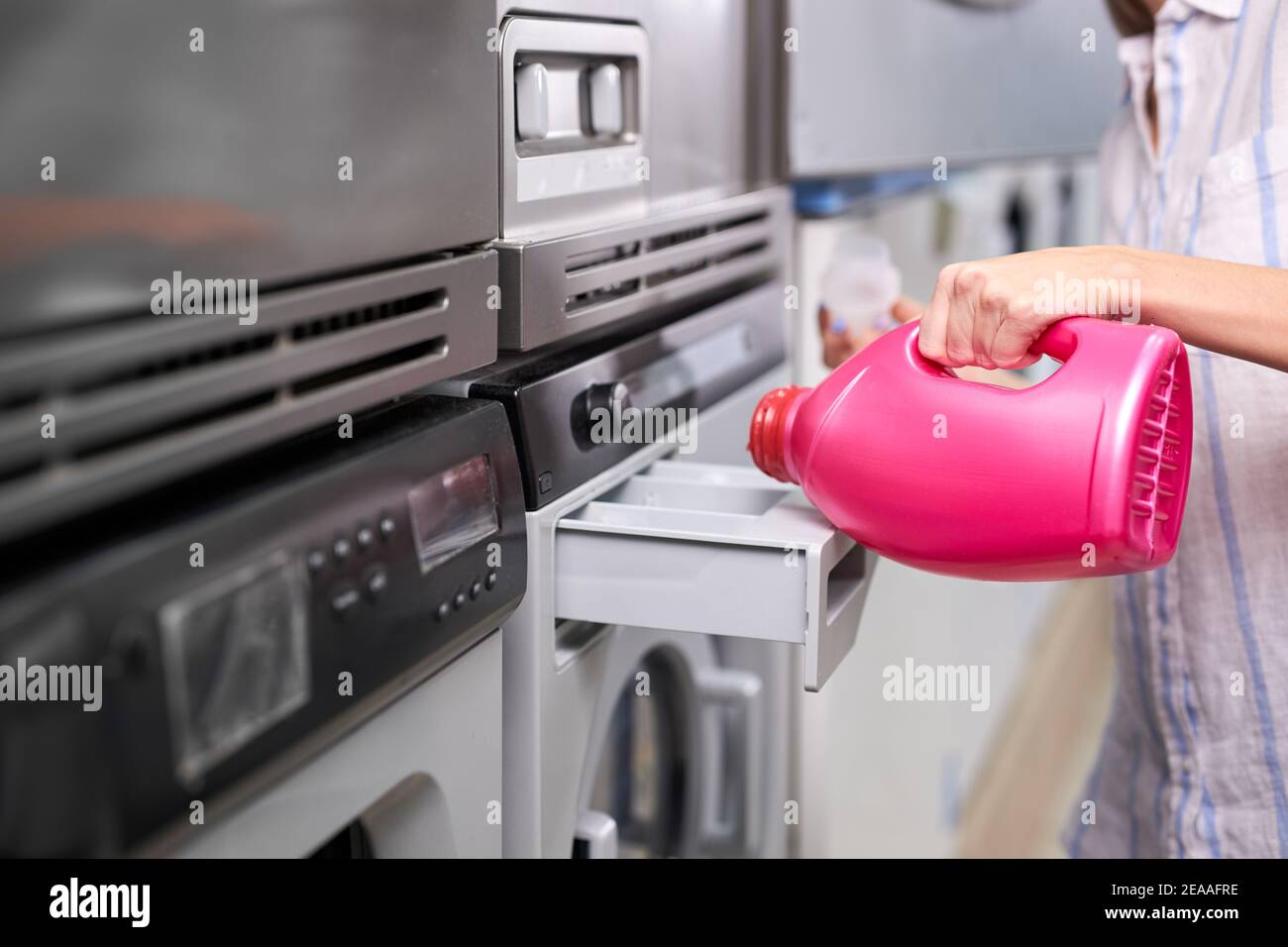 female hand pours a greasy detergent from pink bottle into the washing ...