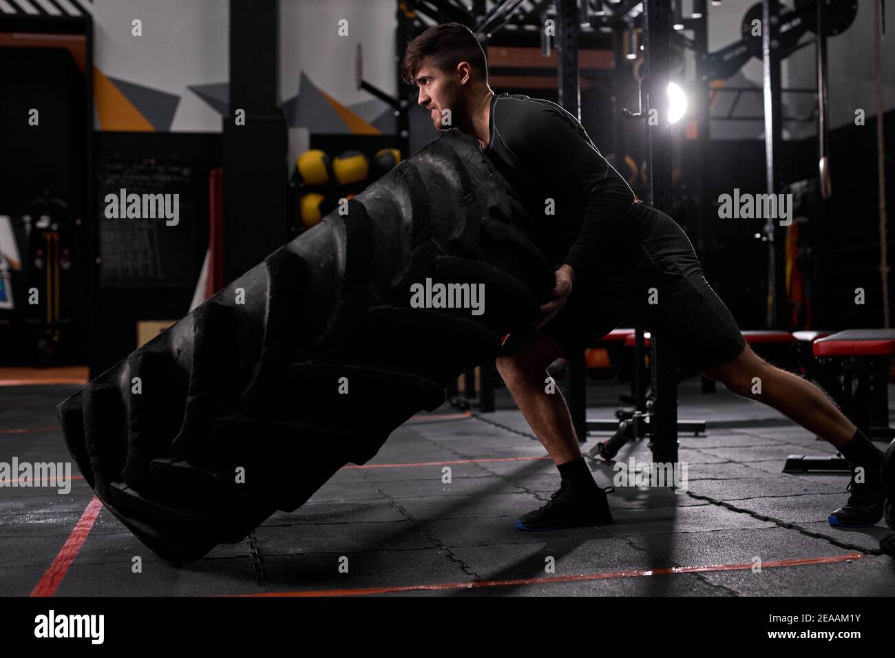 Fit male athlete doing tire-flip exercise indoors in modern gym. Cross ...