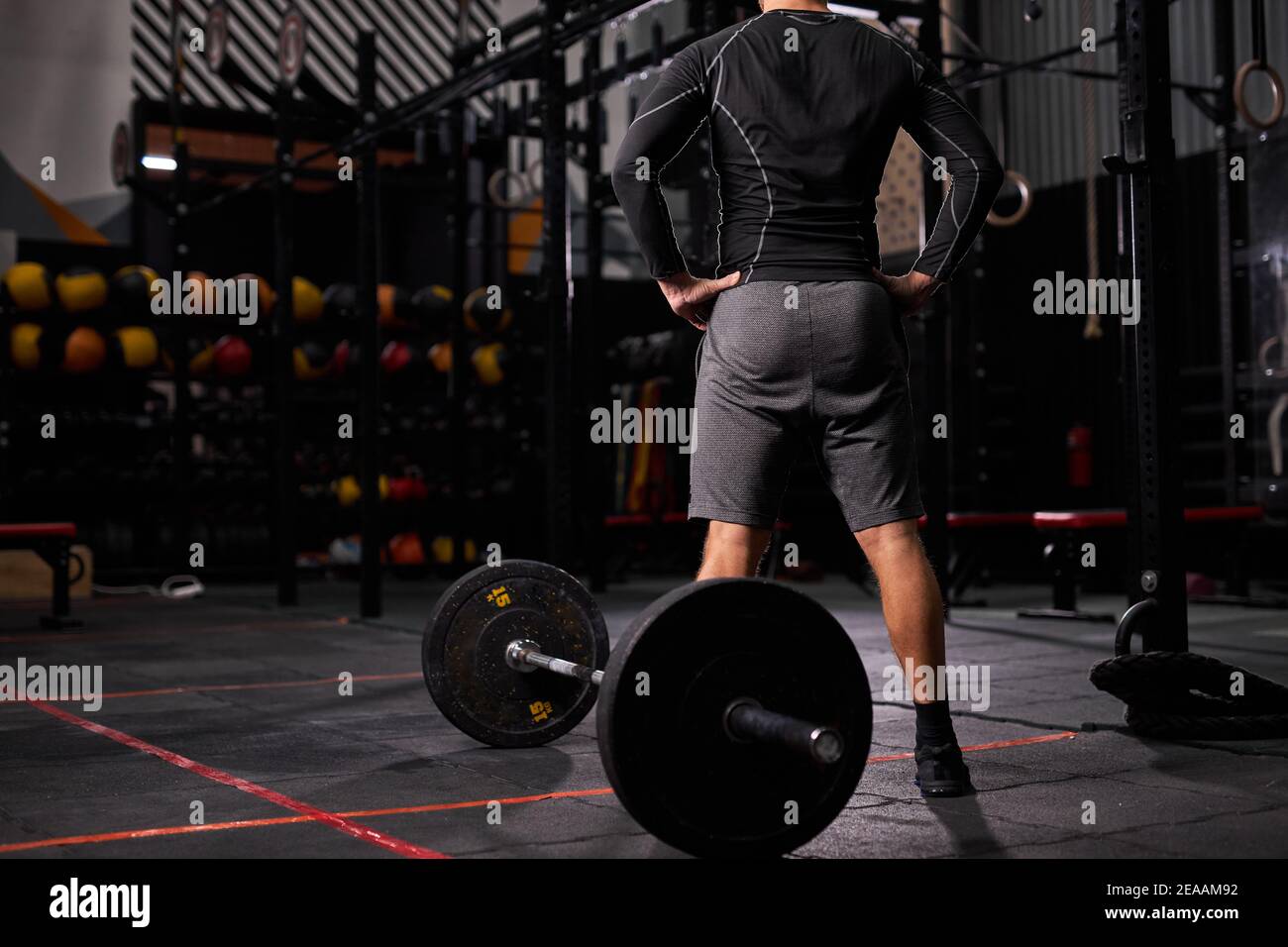 rear view on sportsman standing near barbell taking break, rest. male ...