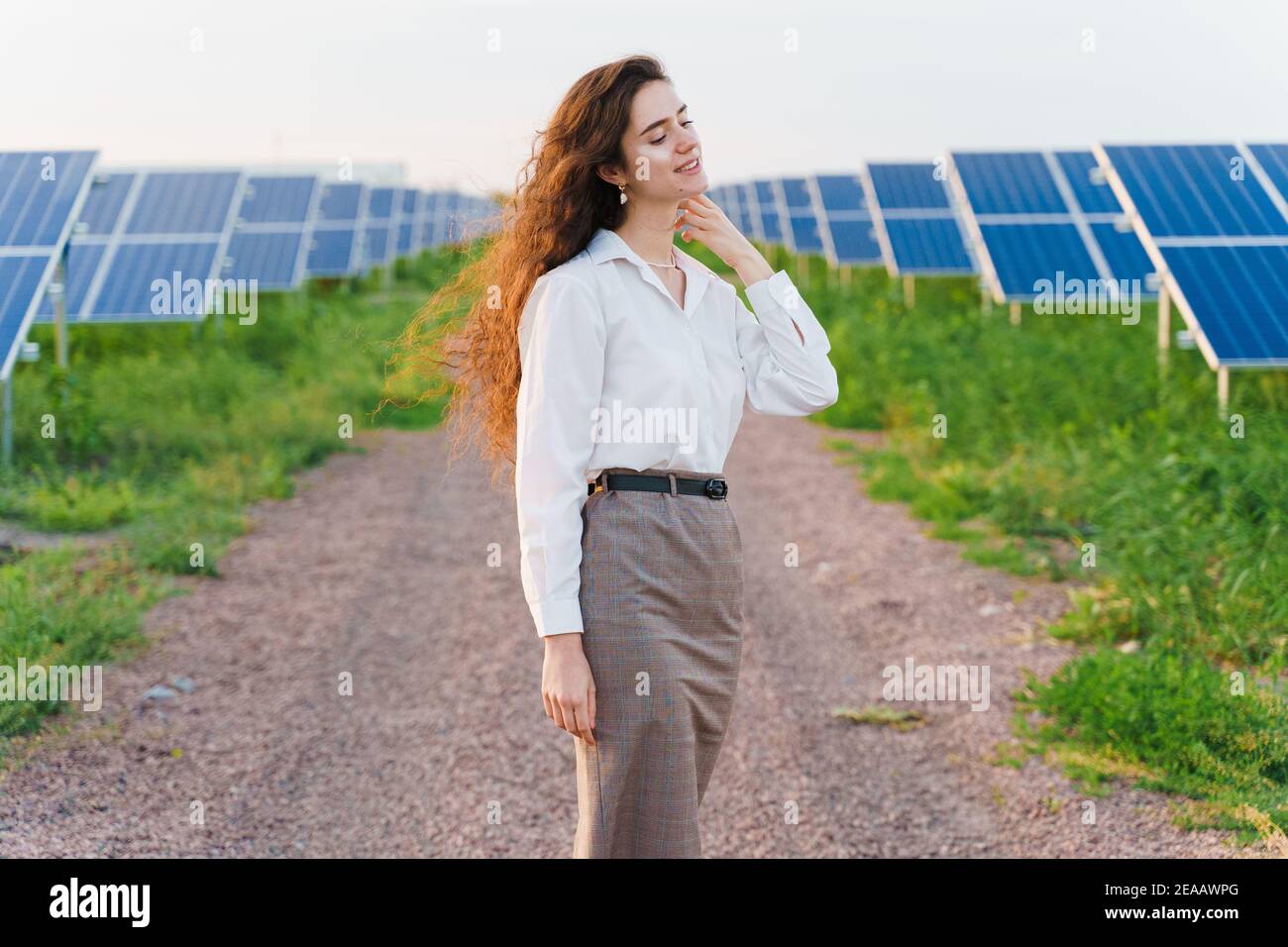 Woman walks near solar panels row on the ground at sunset and smile and ...