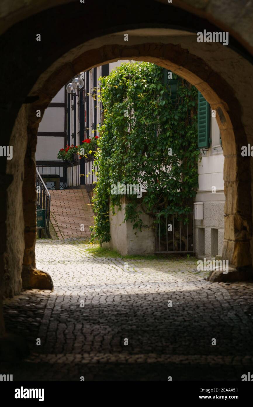 dark medieval archway leads into daylight with truss house and cobble ...