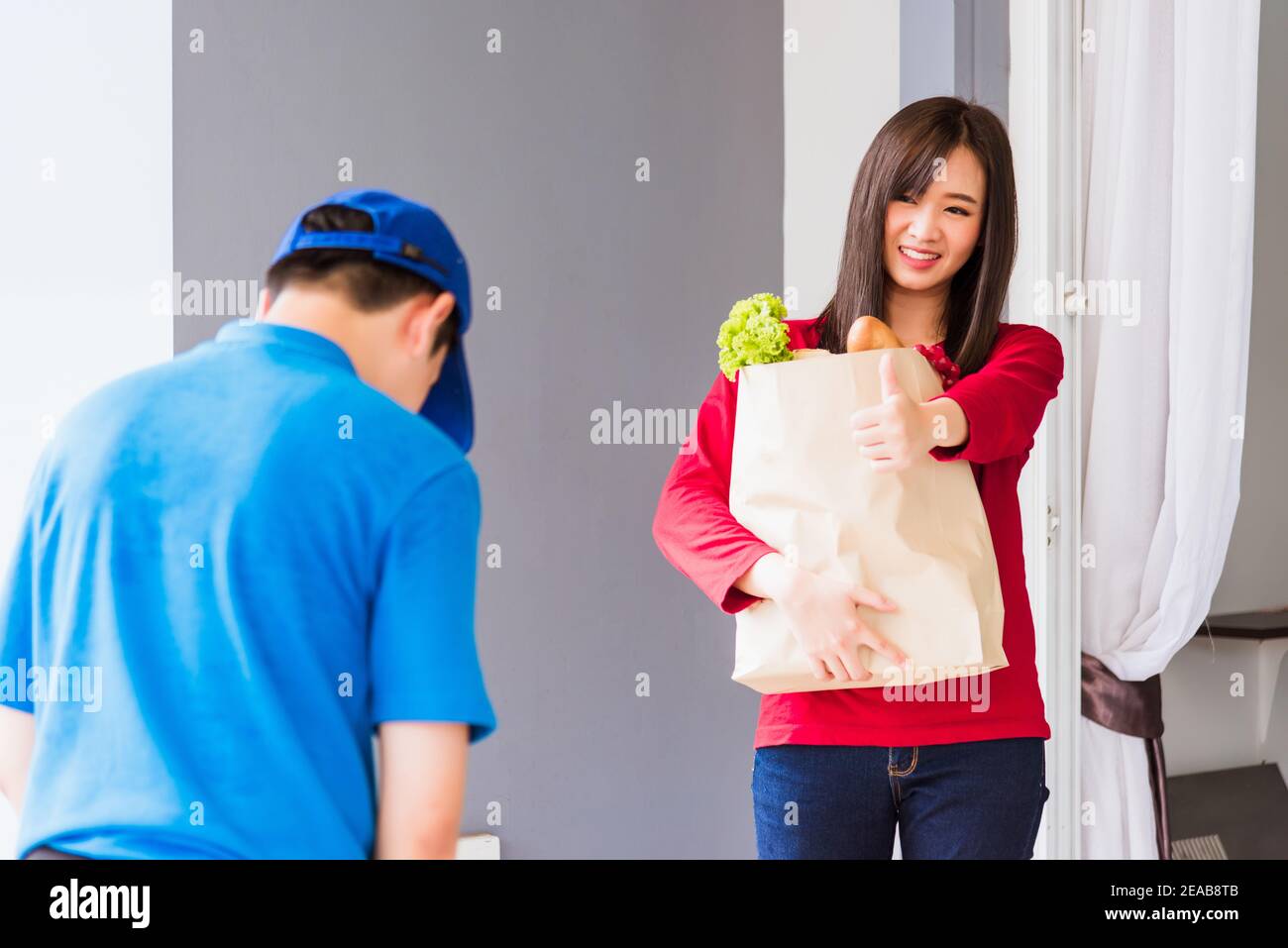 Asian young delivery man in blue uniform making grocery service giving ...
