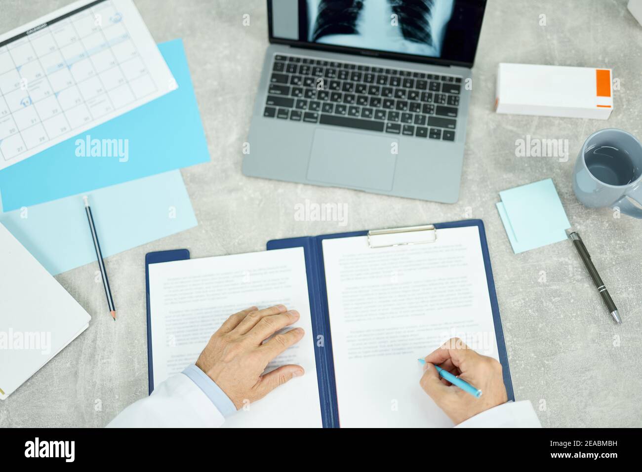 Doctor workplace with laptop and male hands filling in patient chart ...