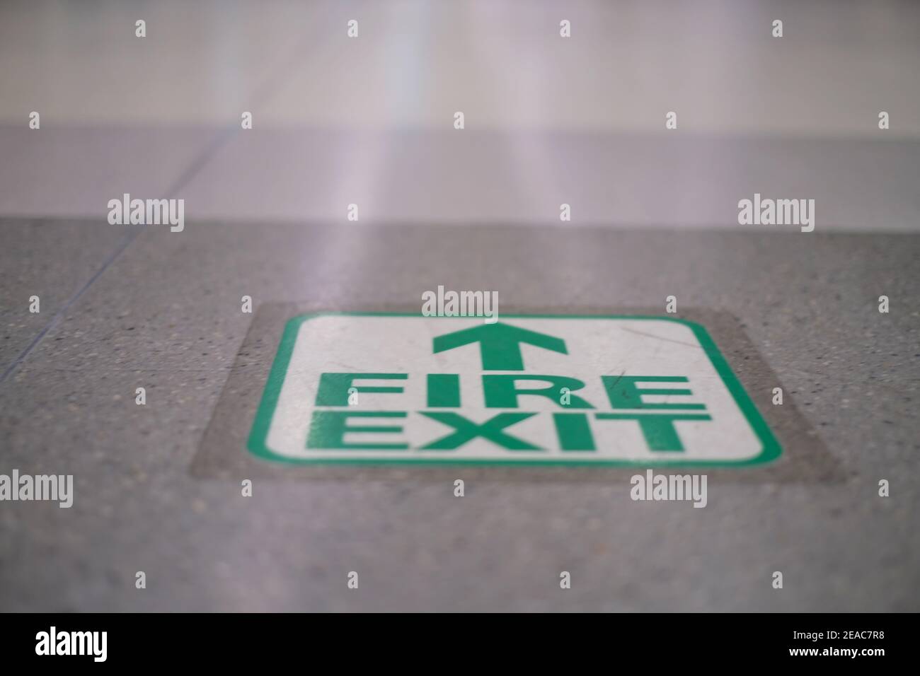 A green fire exit with an arrow on a gray tile floor, pointing to a ...