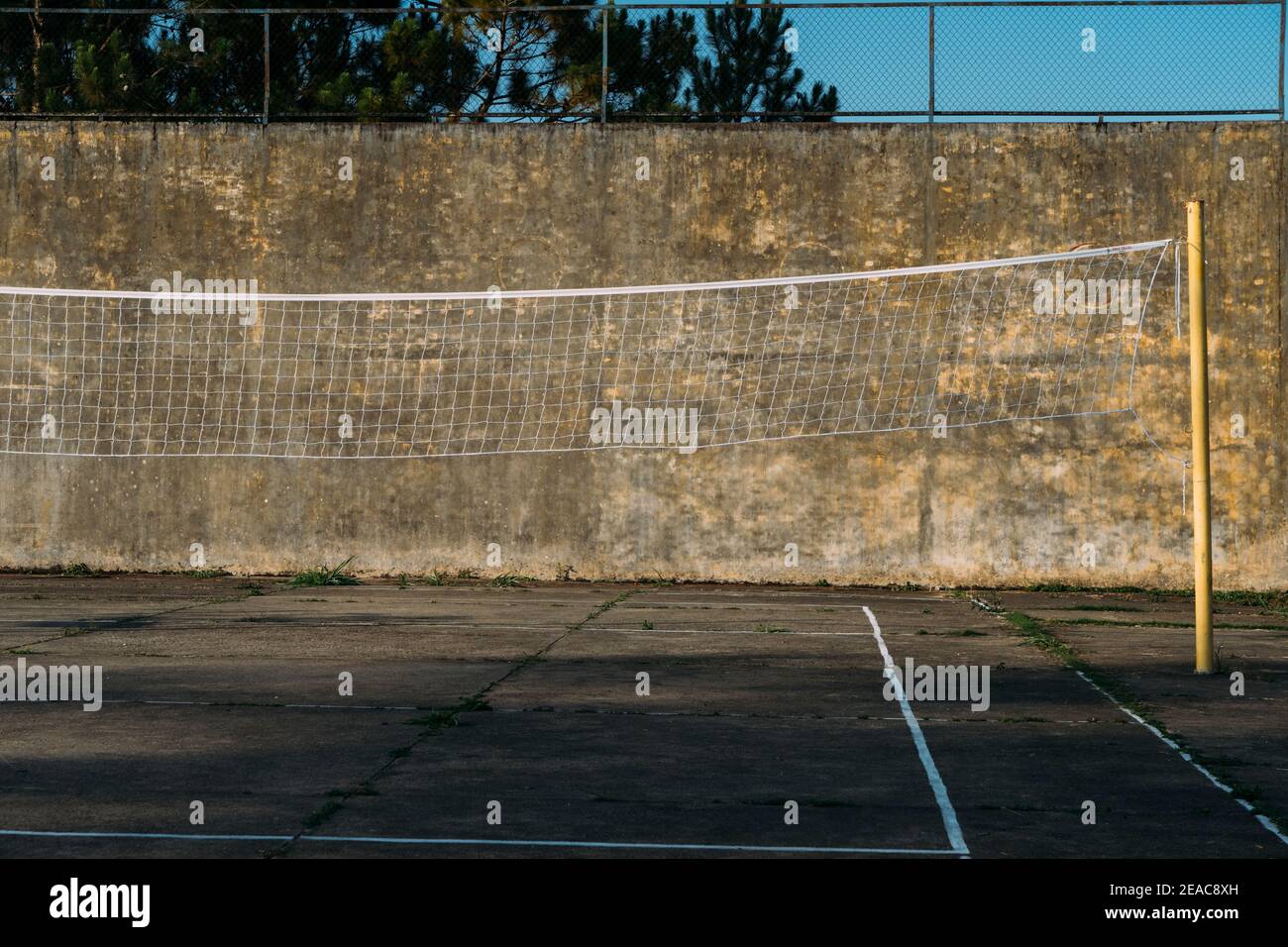 Volleyball net hanging from yellow pole in old, beat-up, cement, court ...