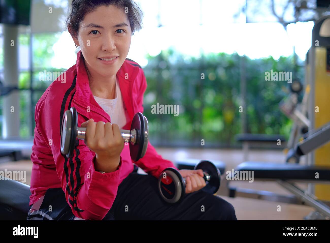 An attractive young Asian woman working out in a gym, lifting weight ...