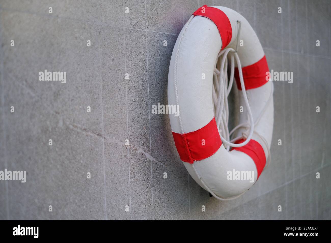 A red and white lifesaver with rope, hanging on a wall by a pool for ...