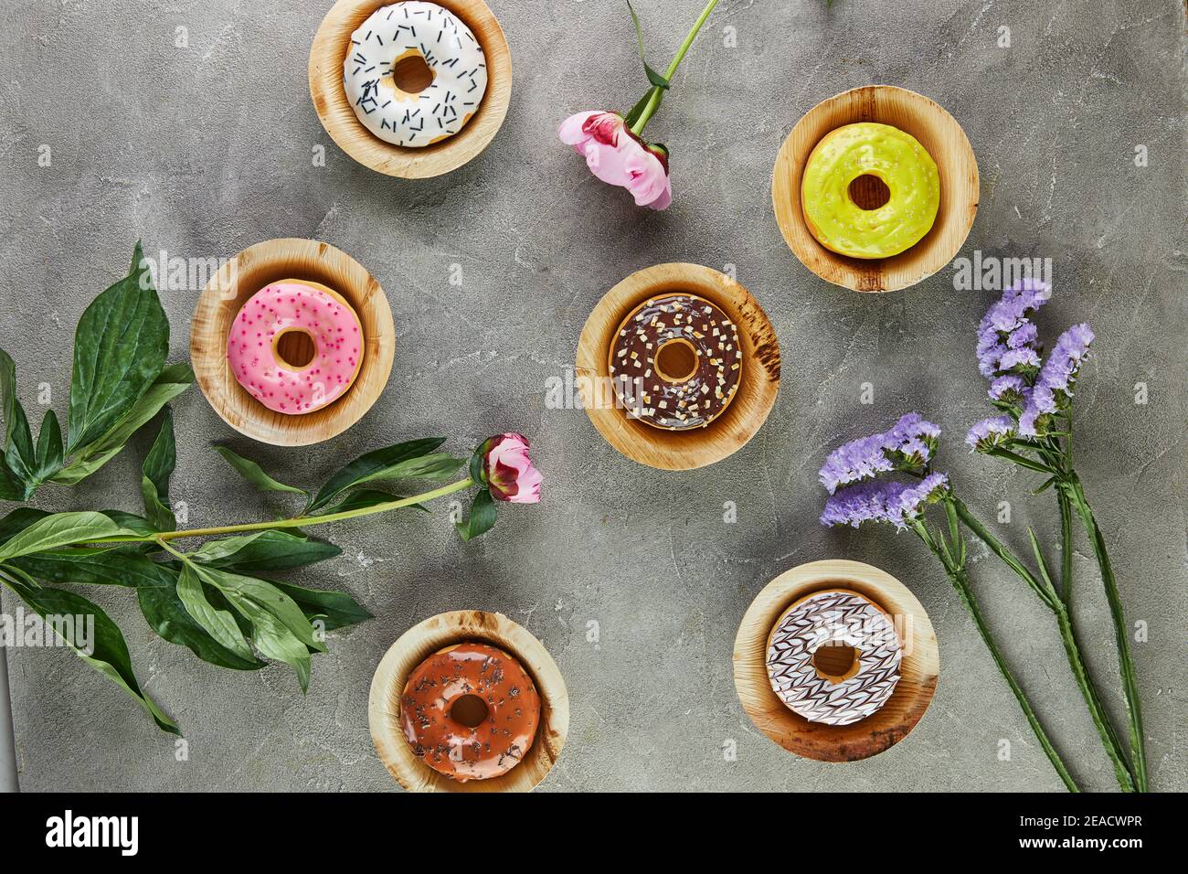 Multicolored donuts with glaze and sprinkles with flowers on a gray ...