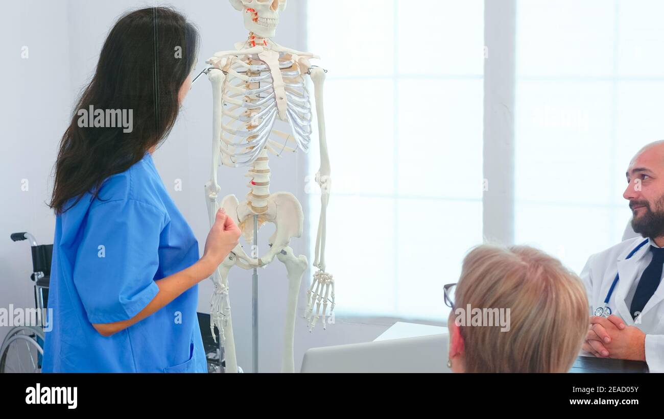 Female nurse demonstrating on skeleton in front of medical surgeons in ...