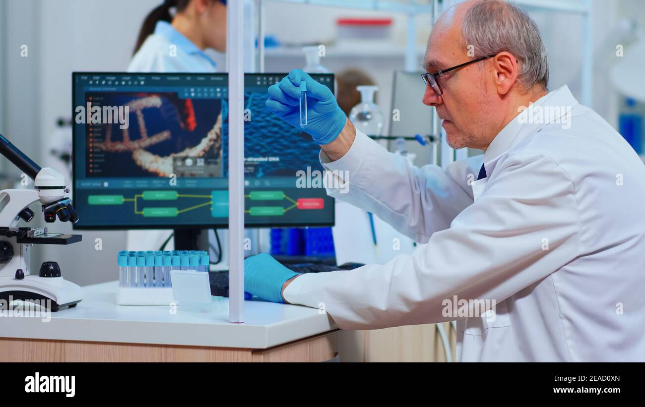Elderly doctor writing on pc datas from test tubes in modern equipped ...