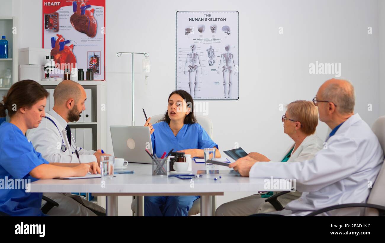 Nurse sitting at conference desk discussing with team during medical ...
