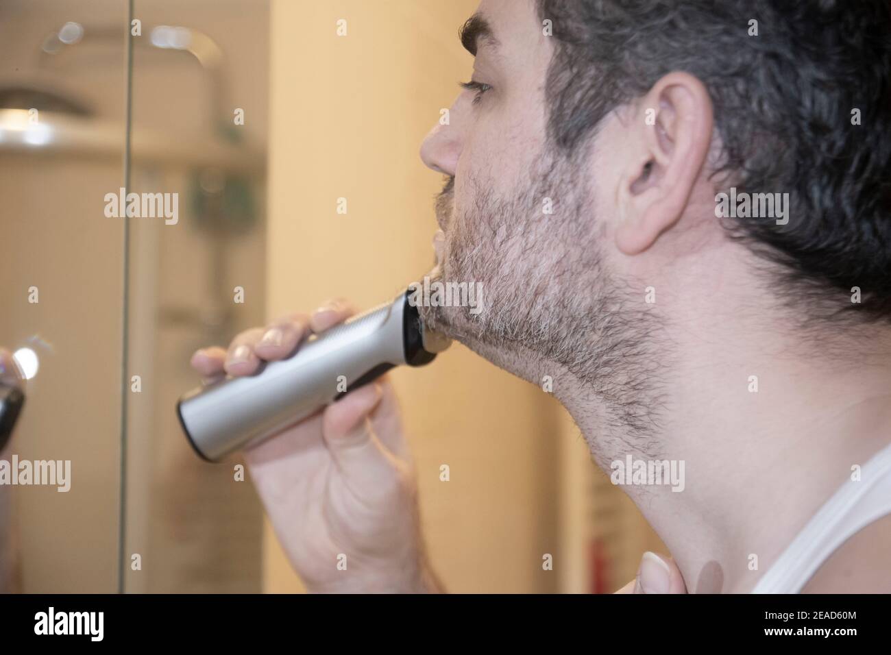 a man shaves his beard with rechargeable machine at home in the ...
