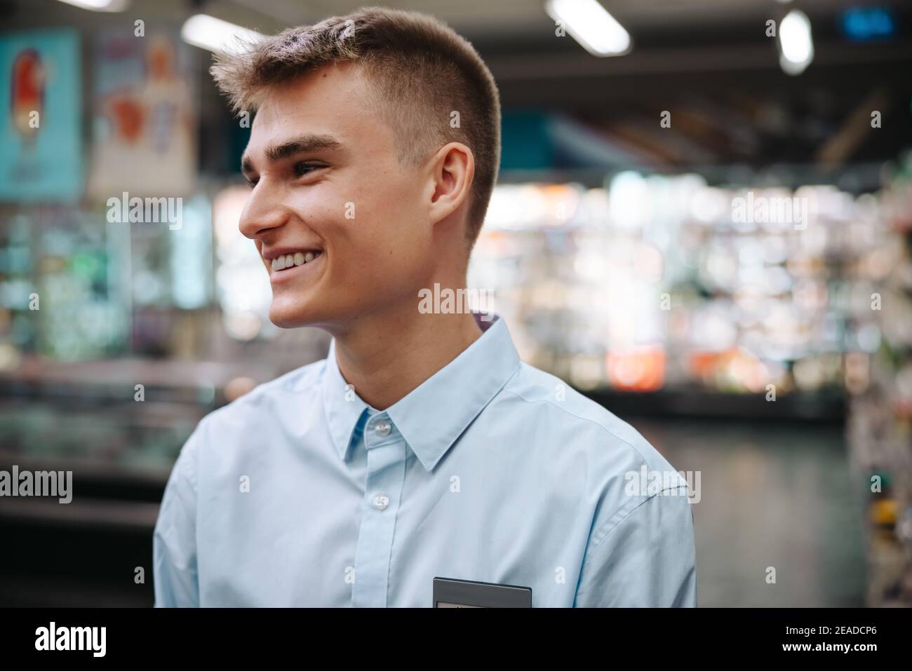 Close-up of a man working in a grocery store. Young worker looking away ...
